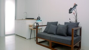 Uma sala de estar moderna com um sofá cinzento, uma mesa de centro e uma pequena mesa lateral com uma chaleira e um alto-falante.