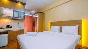 Quarto de hotel com cama, pequeno espaço de cozinha e área de chuveiro.