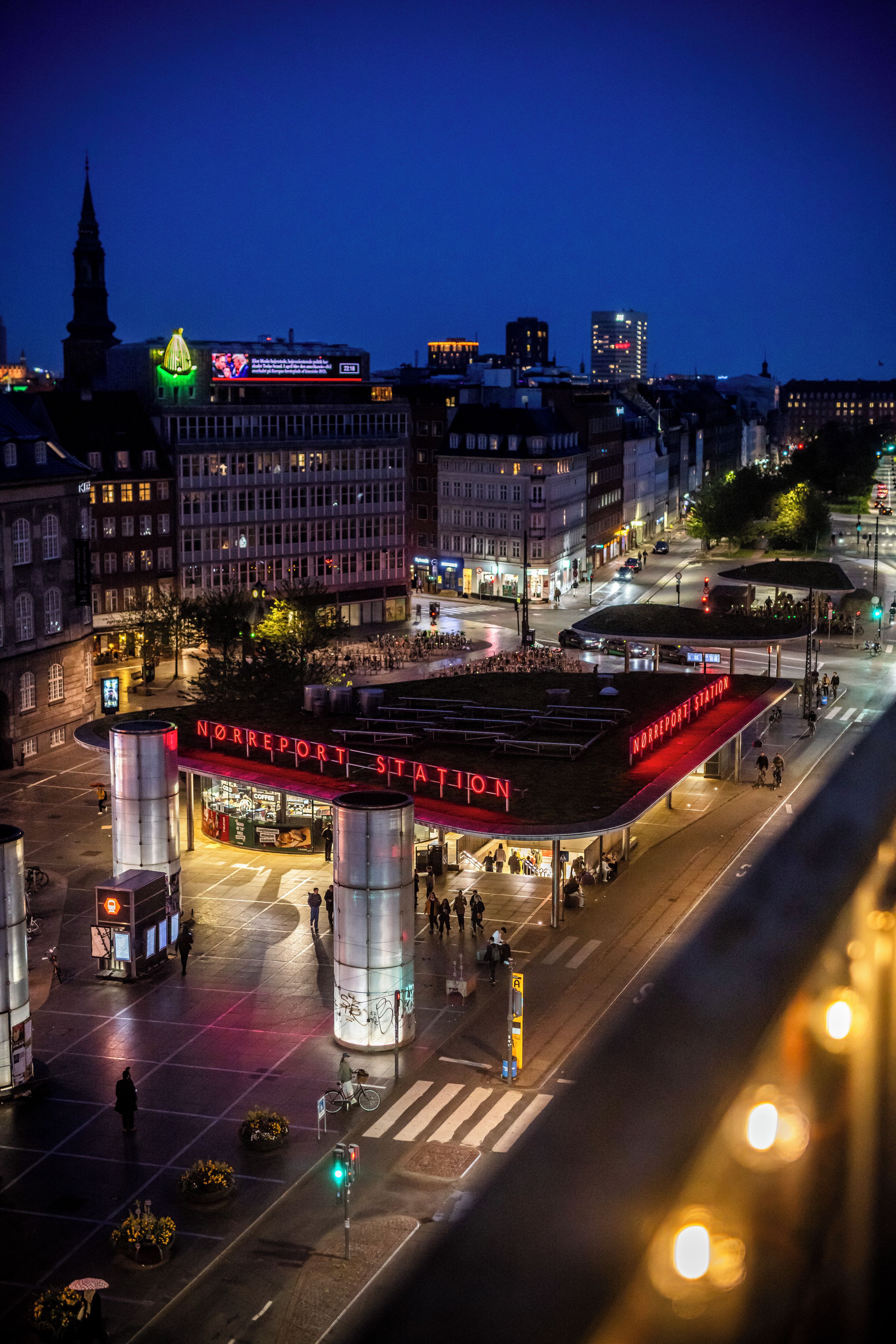 Um cruzamento urbano com um edifício destacado identificado como 'Nørreport Station' e um ponto de tram.