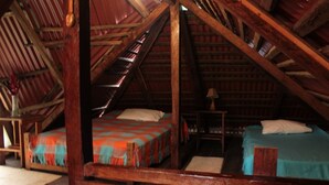 Quarto rústico no sótão, com duas camas, vigas de madeira e teto inclinado.
