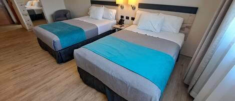 Quarto de hotel com duas camas, cada uma com cabeceira, mesa de cabeceira com abajur e telefone.