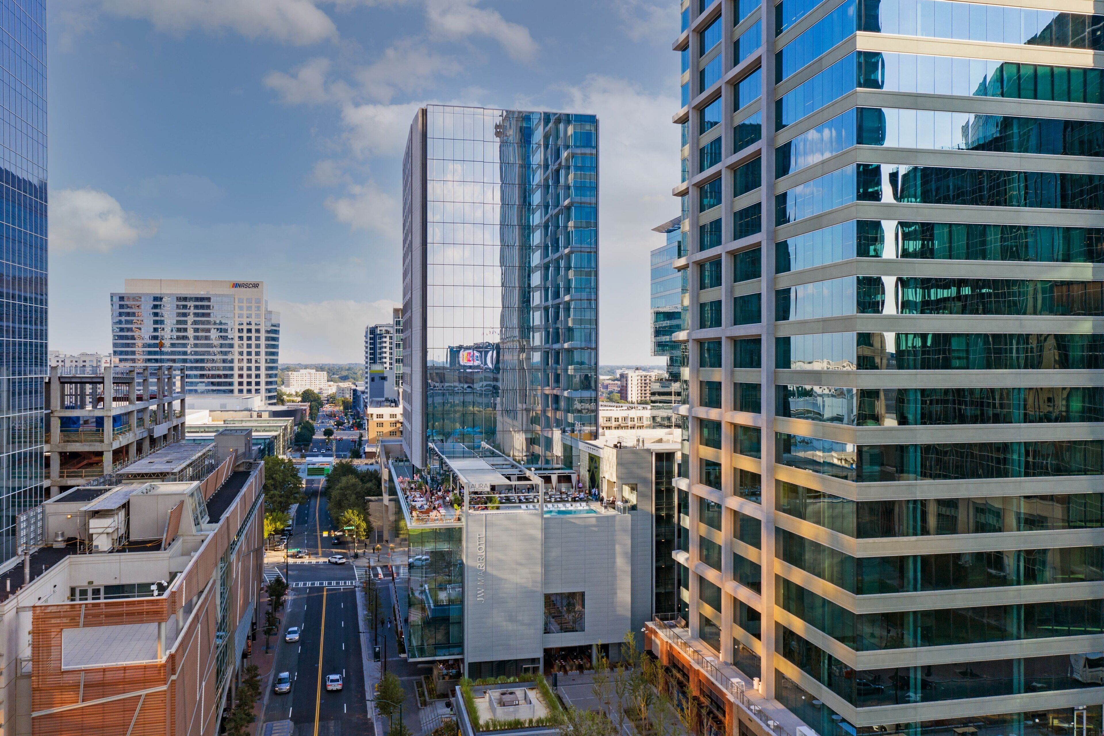 Paisagem urbana moderna com arranha-céus, incluindo um imponente arranha-céu de vidro e um edifício com terraço no topo.