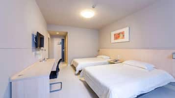 Quarto de hotel com duas camas de solteiro, uma escrivaninha com cadeira, uma TV de tela plana fixada na parede e uma porta que dá para outro cômodo.