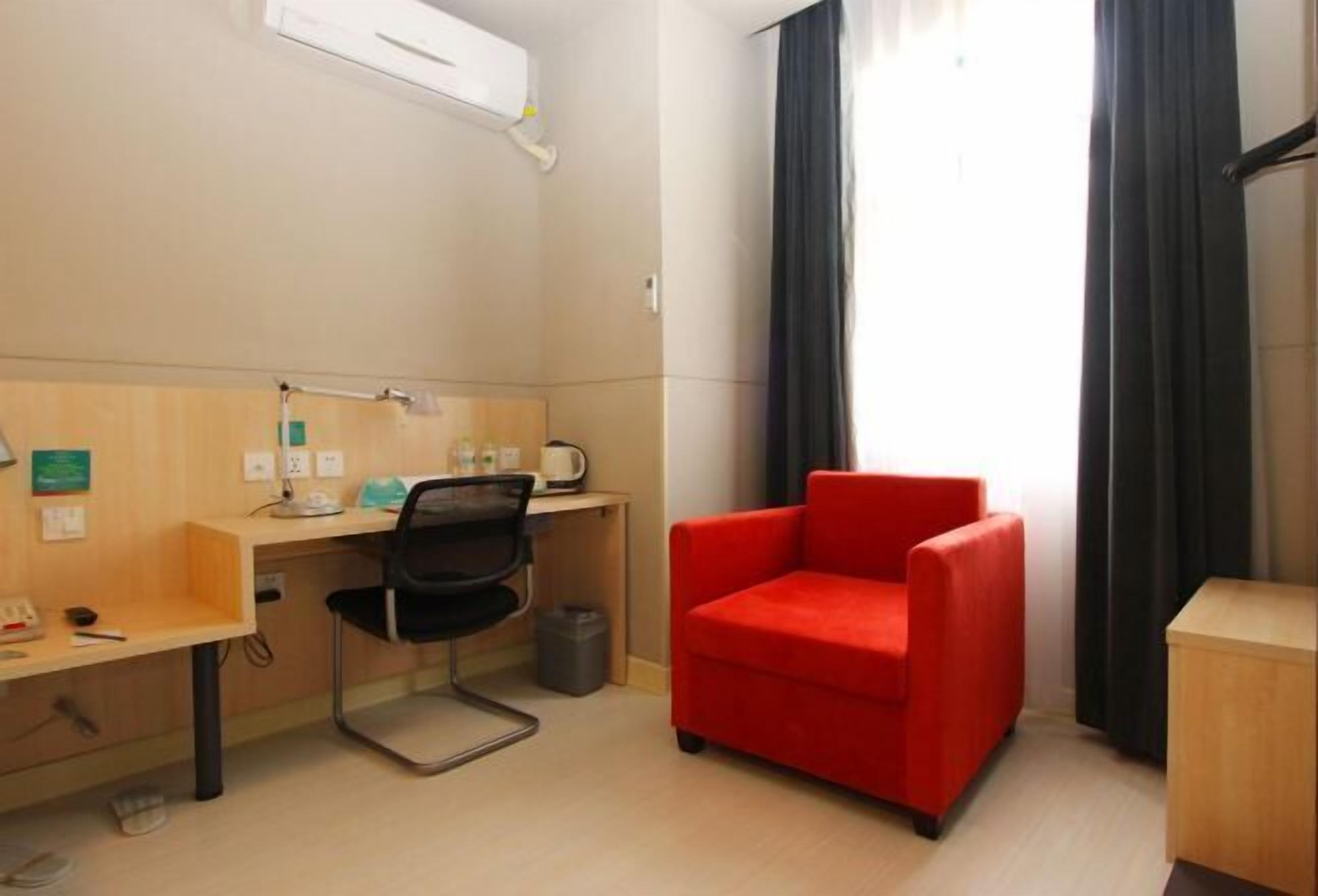 Quarto de hotel com escrivaninha, cadeira e poltrona vermelha.