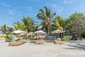 Um resort à beira-mar com espreguiçadeiras de madeira, guarda-sóis e palmeiras.