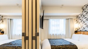 Quarto de hotel com duas camas, uma televisão de tela plana na parede, uma janela com cortinas finas e um papel de parede estampado.