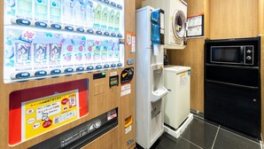 Máquina de vendas com diversas opções de bebidas, uma pequena geladeira e um micro-ondas em um quarto com paredes de madeira.