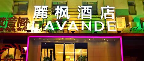 Hotel com placa de destaque com a palavra 'LAVANDE' e fachada moderna com janelas grandes e um letreiro de neon.