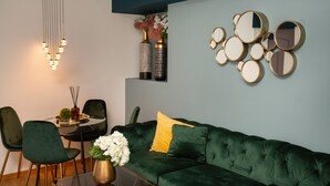 Uma sala de estar moderna com um sofá verde, uma mesa de centro redonda e um espaço de jantar com cadeiras e uma pequena mesa.