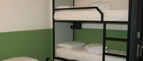 Uma cama beliche com roupa de cama e almofadas brancas, uma parede verde e uma porta à direita.
