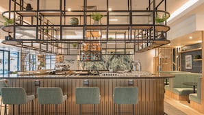 Uma área de bar com ilha central, banquetas e um espaço de estar com cadeiras estofadas.