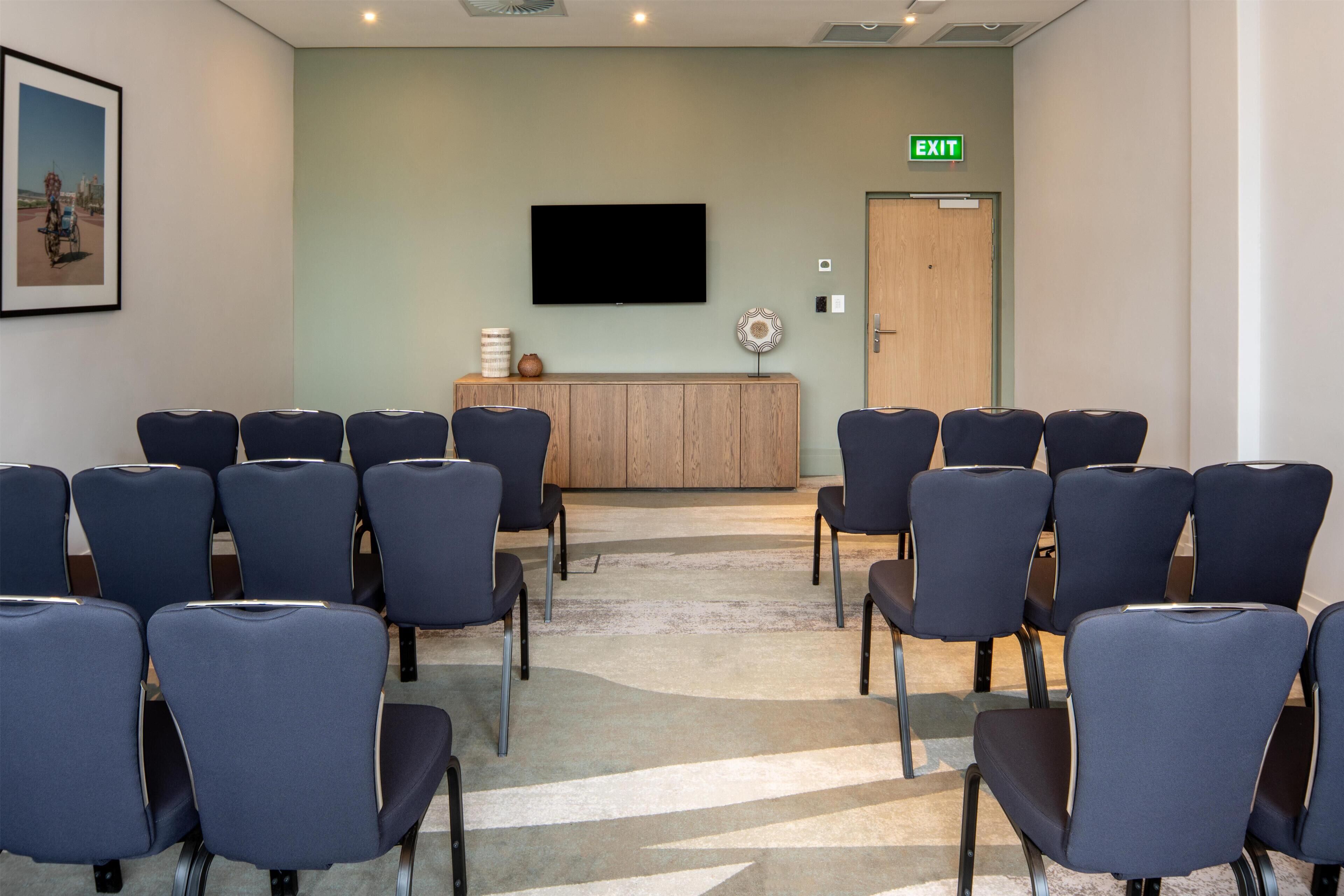 Uma sala de conferências com uma TV de tela plana, um pódio de madeira e uma porta de saída.