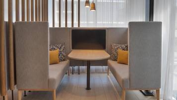 Quarto moderno com uma mesa redonda, duas poltronas cinzentas e um sofá com almofadas estampadas.