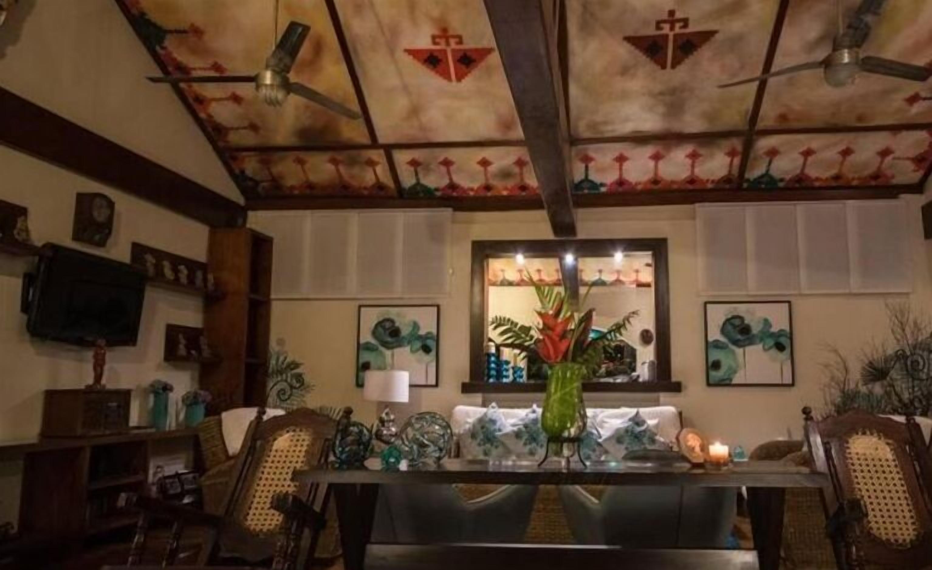 Uma área de refeições com teto alto, azulejos decorativos no teto e uma mesa central com cadeiras.