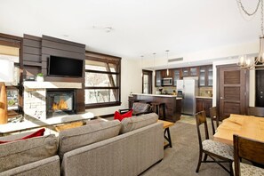 Uma sala de estar moderna com lareira, TV e área de jantar com mesa e cadeiras de madeira.