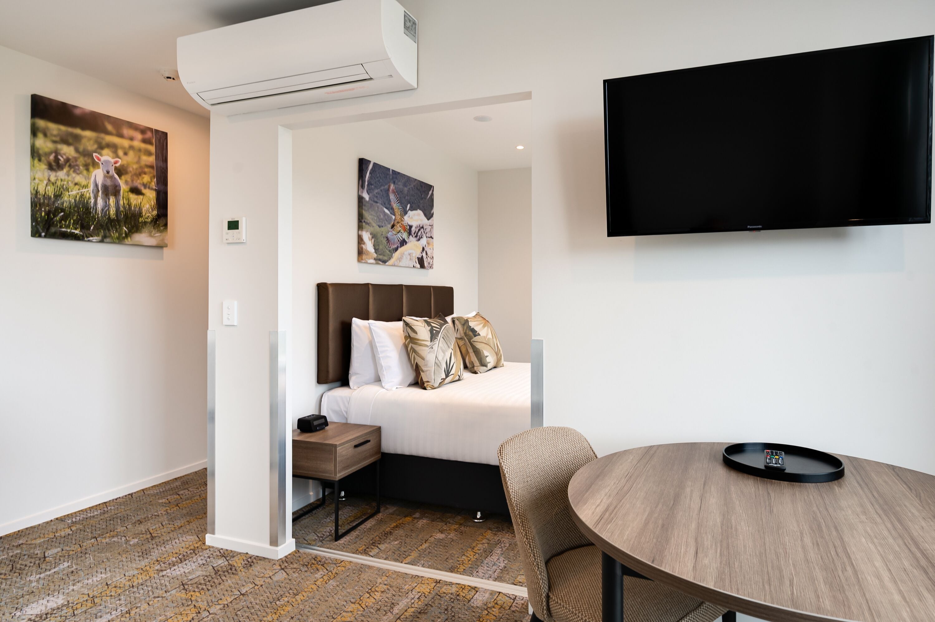 Quarto de hotel moderno com uma cama, uma televisão de tela plana e uma mesa de jantar redonda.