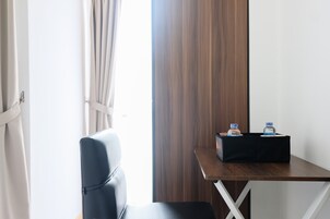 Quarto de hotel com uma escrivaninha de madeira, uma poltrona de couro preto e uma pequena mesa com duas garrafas de água.