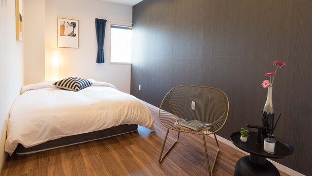 Quarto moderno com cama, uma cadeira, uma mesinha com um vaso e janela com cortinas.