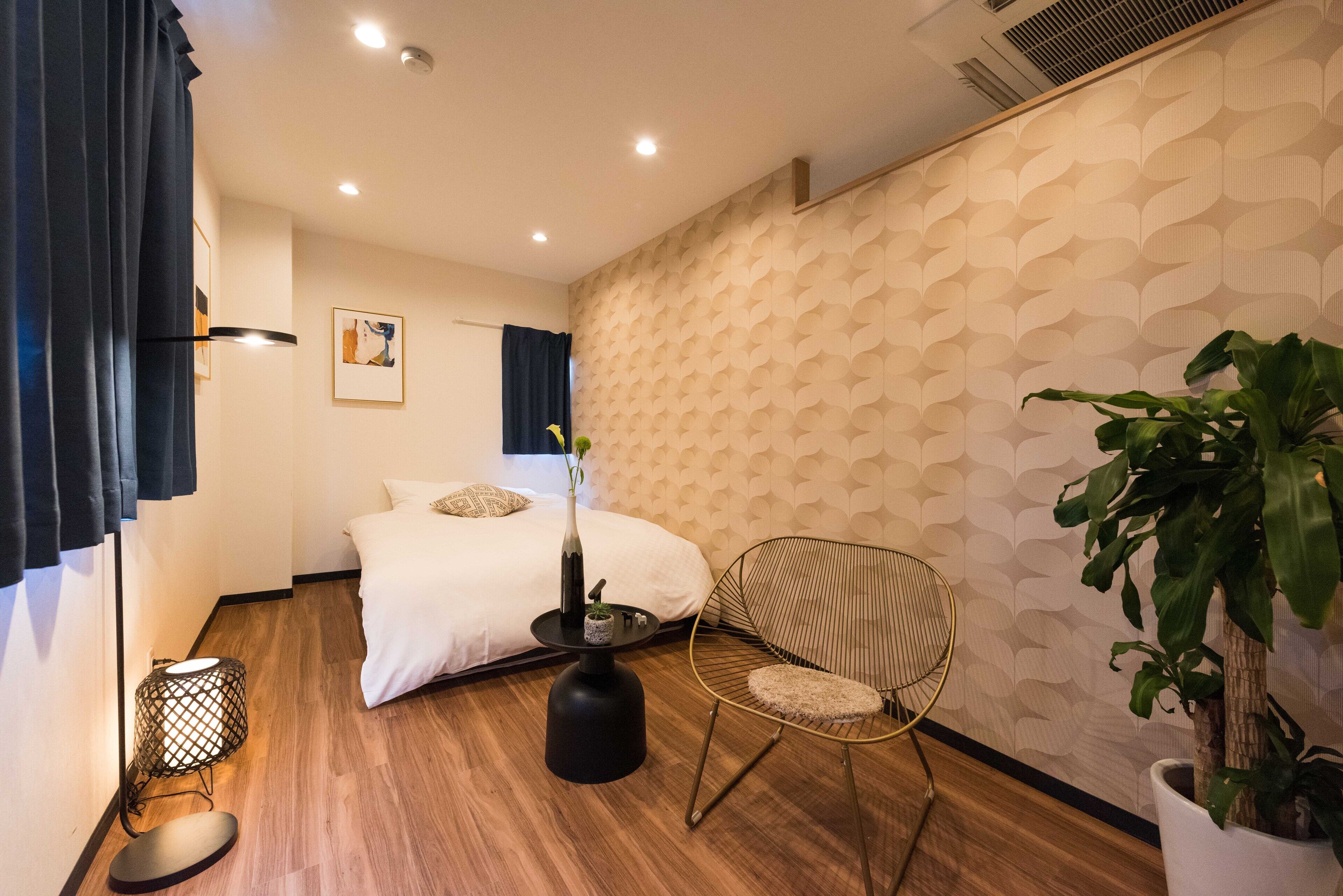 Quarto com cama, poltrona, planta em vaso e parede com padrão geométrico.