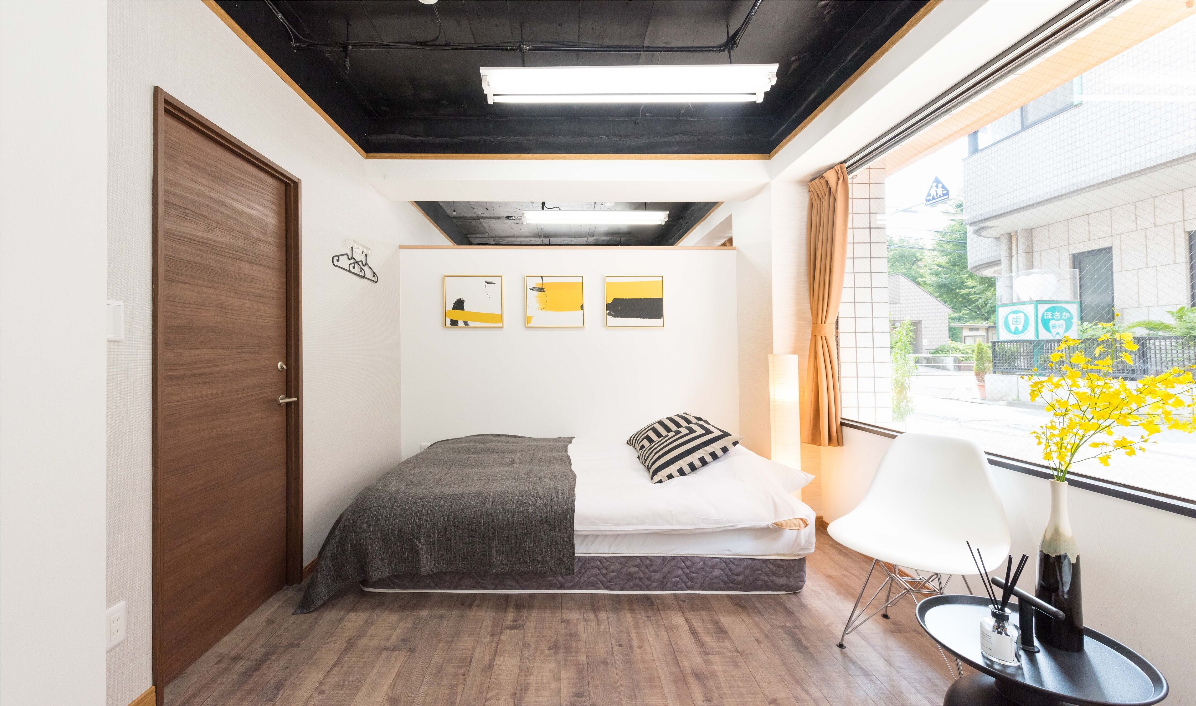 Quarto com cama, mesa de cabeceira, cadeira, janela com cortinas e uma obra de arte na parede.