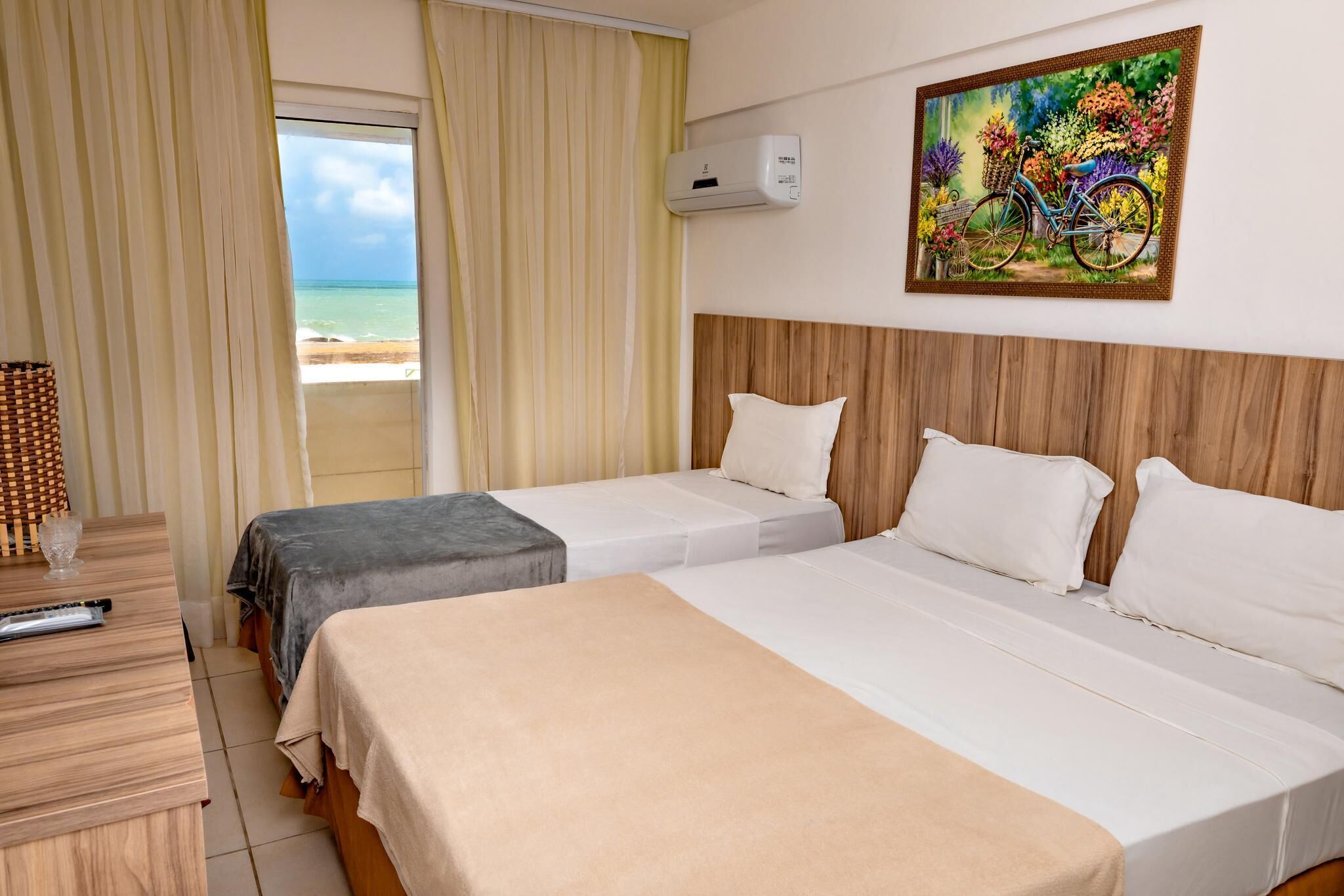 Quarto de hotel com duas camas, vista para a praia e um quadro na parede.