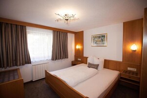 Quarto de hotel com cama de madeira, mesa de cabeceira, luminária e janela com cortinas.