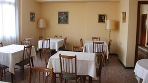 Uma área de refeições com mesas e cadeiras, saídas de ar condicionado e obras de arte emolduradas nas paredes.
