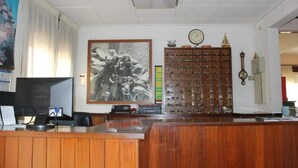 Uma área de recepção com uma mesa de madeira, uma fotografia grande emoldurada, um relógio e uma vitrine fixada na parede.