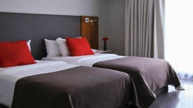 Quarto de hotel com duas camas, cada uma com colcha marrom e almofadas vermelhas.