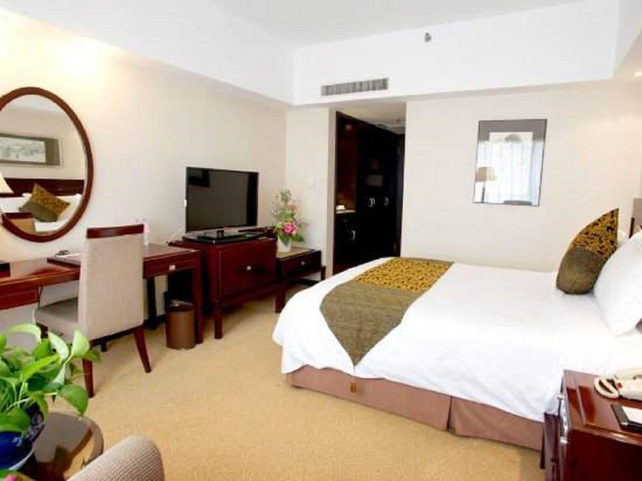 Quarto de hotel com cama, escrivaninha, cadeira, televisão e espelho.