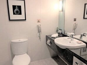 Uma casa de banho moderna com sanita branca, uma pia com espelho e um quadro emoldurado na parede.