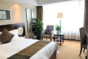 Quarto de hotel com uma cama grande, uma cadeira, uma mesinha e um abajur.