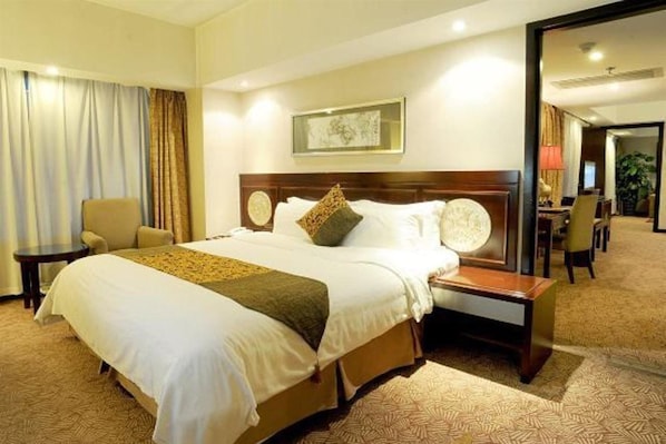 Quarto de hotel com uma cama grande, mesa de cabeceira, uma cadeira e uma escrivaninha.