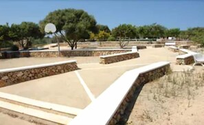 Quadra de basquete ao ar livre com paredes de pedra e árvores ao fundo.