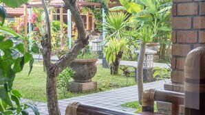 Um jardim com um vaso de pedra, uma árvore pequena e um muro de tijolos.