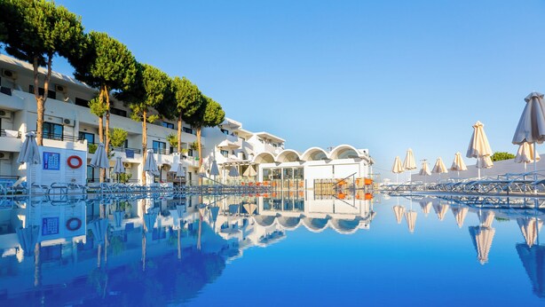 Resort com piscina transparente, edifícios brancos e guarda-sóis.