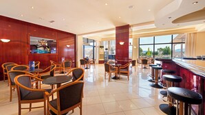 Um hall de hotel com mobiliário de madeira, área de bar e janelas amplas.