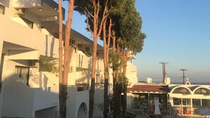 Um edifício moderno com uma fileira de árvores altas, mesas ao ar livre e céu limpo.