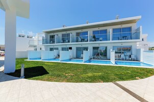 Um edifício moderno de dois andares com piscina, varandas e áreas de estar ao ar livre.