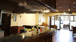 Uma área de bar com balcão polido, diversas bebidas e um lustre.