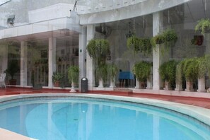 Piscina com vista desobstruída para um edifício com colunas e plantas pendentes.
