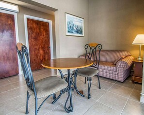 Uma sala de jantar com uma mesa redonda e quatro cadeiras, um sofá estampado, uma porta e um quadro na parede.