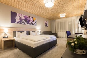 Quarto de hotel moderno com uma cama grande, uma escrivaninha, uma cadeira e uma televisão.