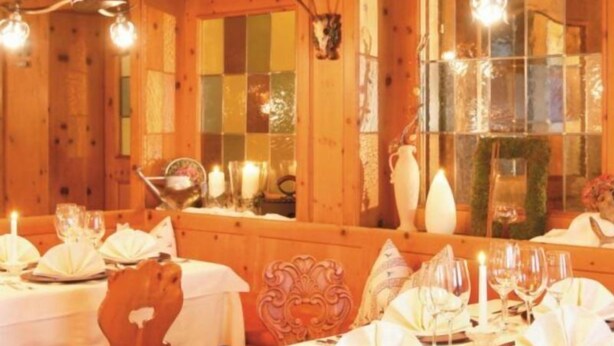 Uma sala de jantar de madeira bem iluminada, com mesas postas para uma refeição, com um candelabro e elementos decorativos.