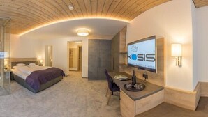 Quarto de hotel moderno com teto curvo, uma cama, uma escrivaninha e uma TV exibindo o nome do hotel.
