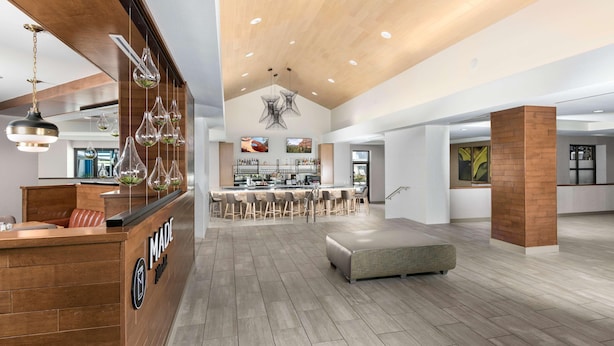 Um amplo hall de hotel com balcão de recepção, área de bar e espaço para refeições.