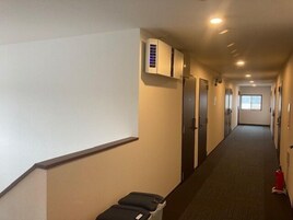 Um corredor de hotel com piso coberto por carpete, uma lixeira e um extintor de incêndio.