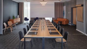 Uma sala de conferências com uma mesa comprida, cadeiras, tela de projetor e um sofá.