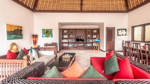Uma sala de estar ampla com pé direito alto, televisão, estantes de livros e um espaço de refeições com cadeiras e mesa.