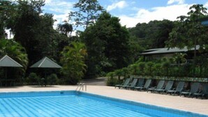 Piscina com superfície de água azul e límpida, rodeada por espreguiçadeiras e áreas com sombra.